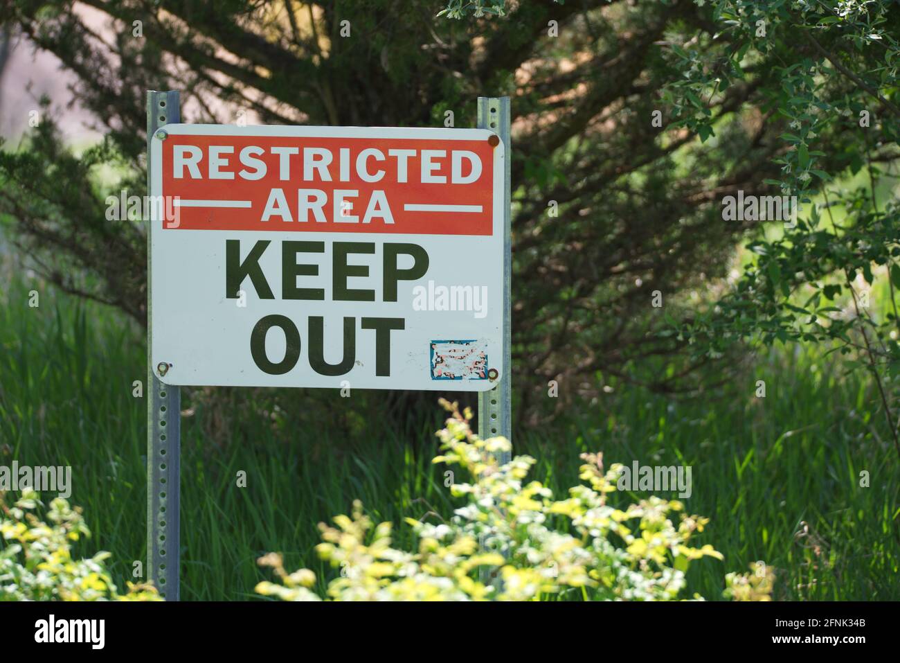 Closeup of a "Restricted Area, Keep out" sign in a field under the sun ...