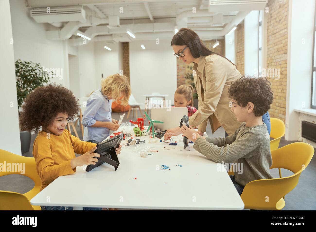 Diverse children using gadgets while learning how to assemble robot ...
