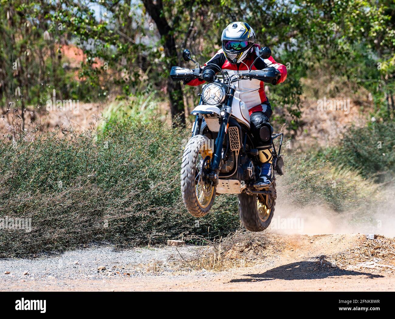 man jumping his scrambler type motorcycle on dirt track in Thailand ...