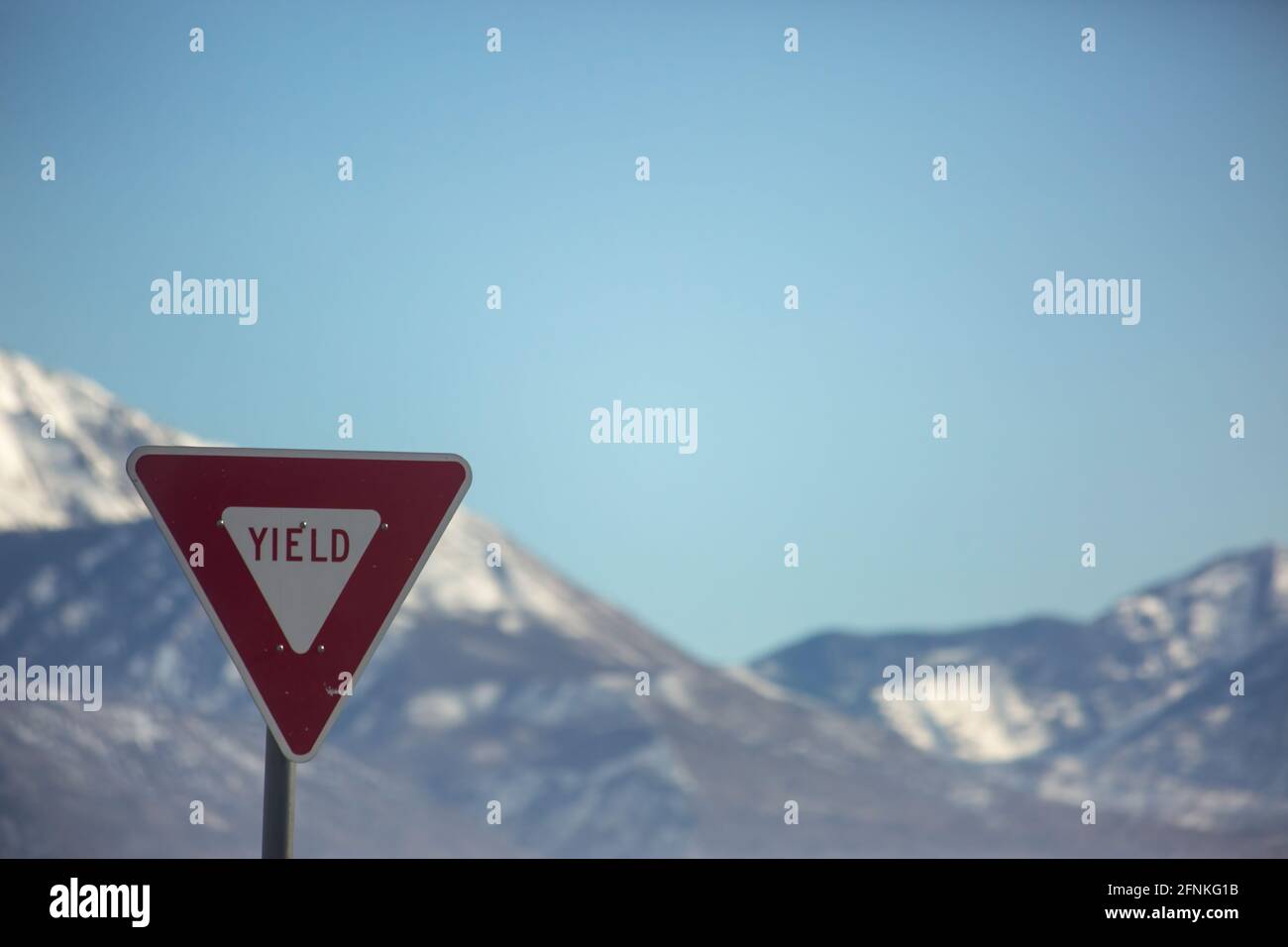 Selective focus of a yield sign in snowy mountains under a clear sky ...