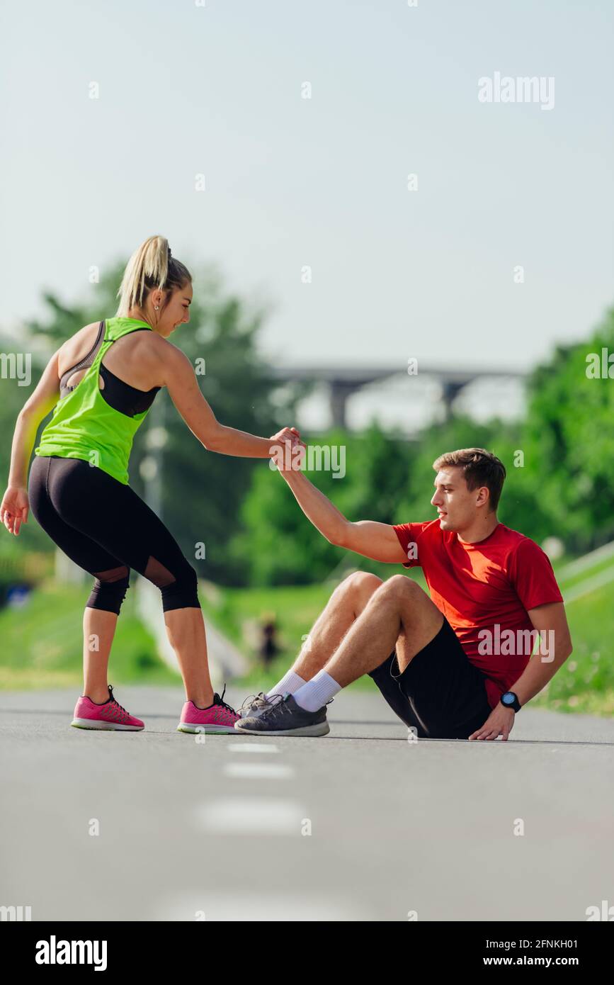 Attractive female helping her male running partner to get up from ...
