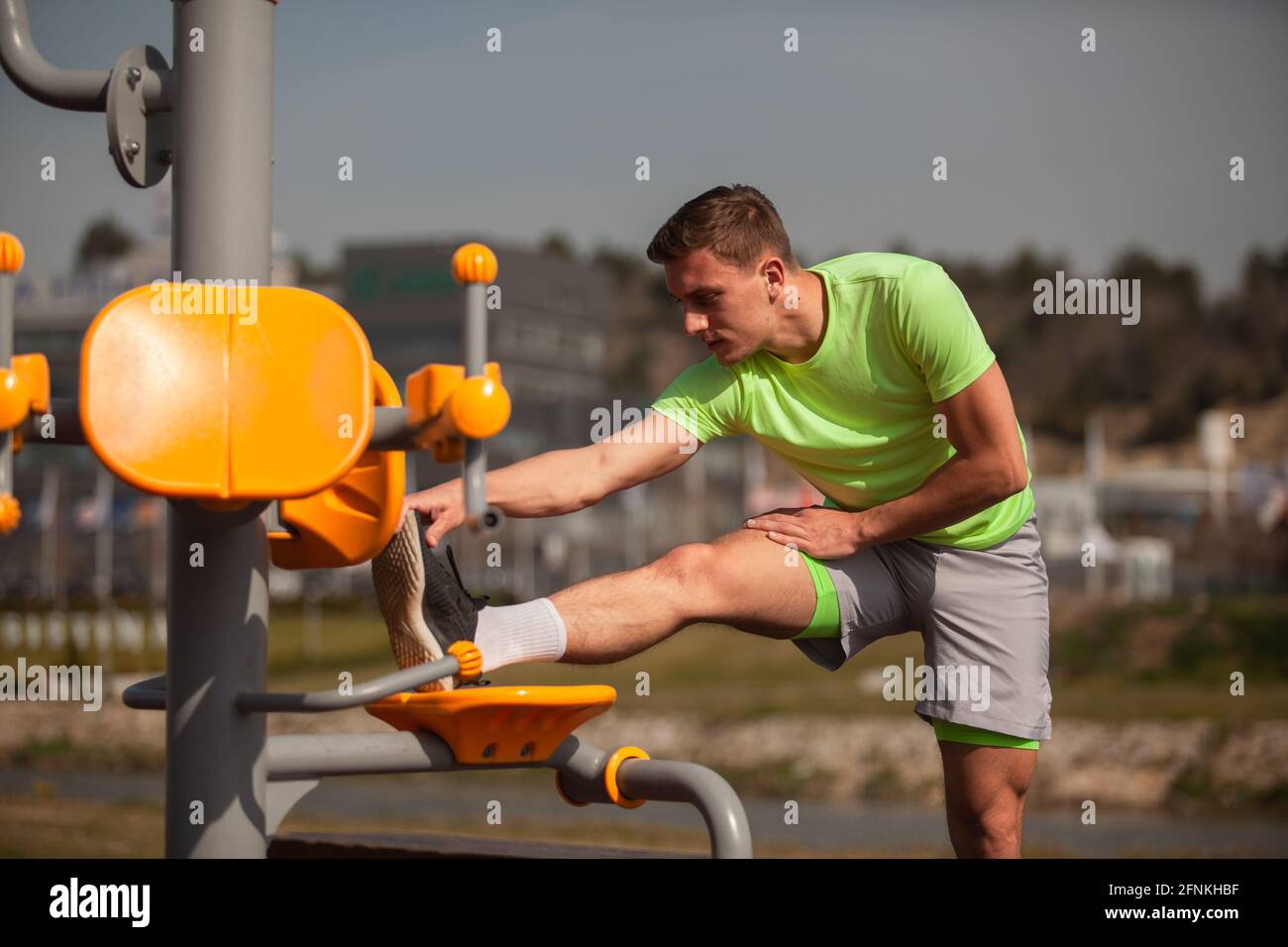 Male sportsman is stretching his leg while warming it up at the same ...