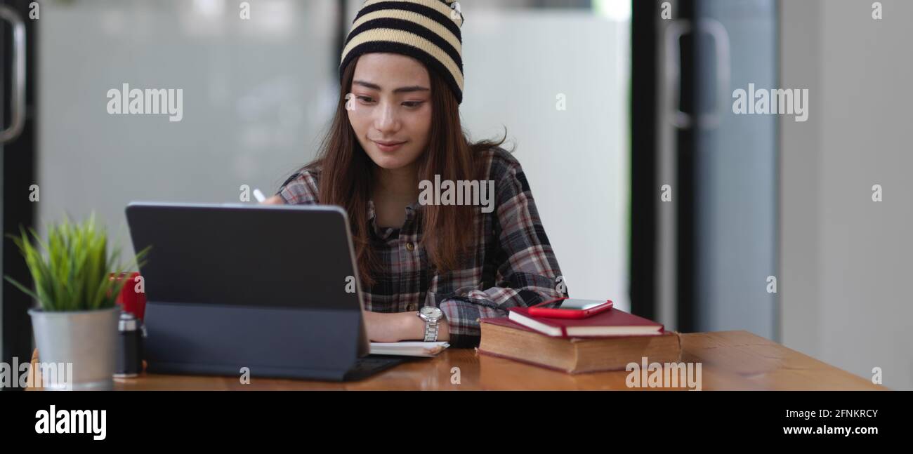 Portrait of female teenager doing assignment with tablet, stationery ...
