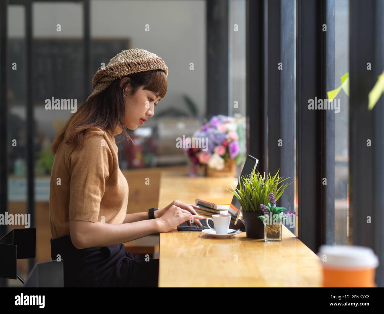 Side view of female teenager doing homework with tablet on wooden bar ...