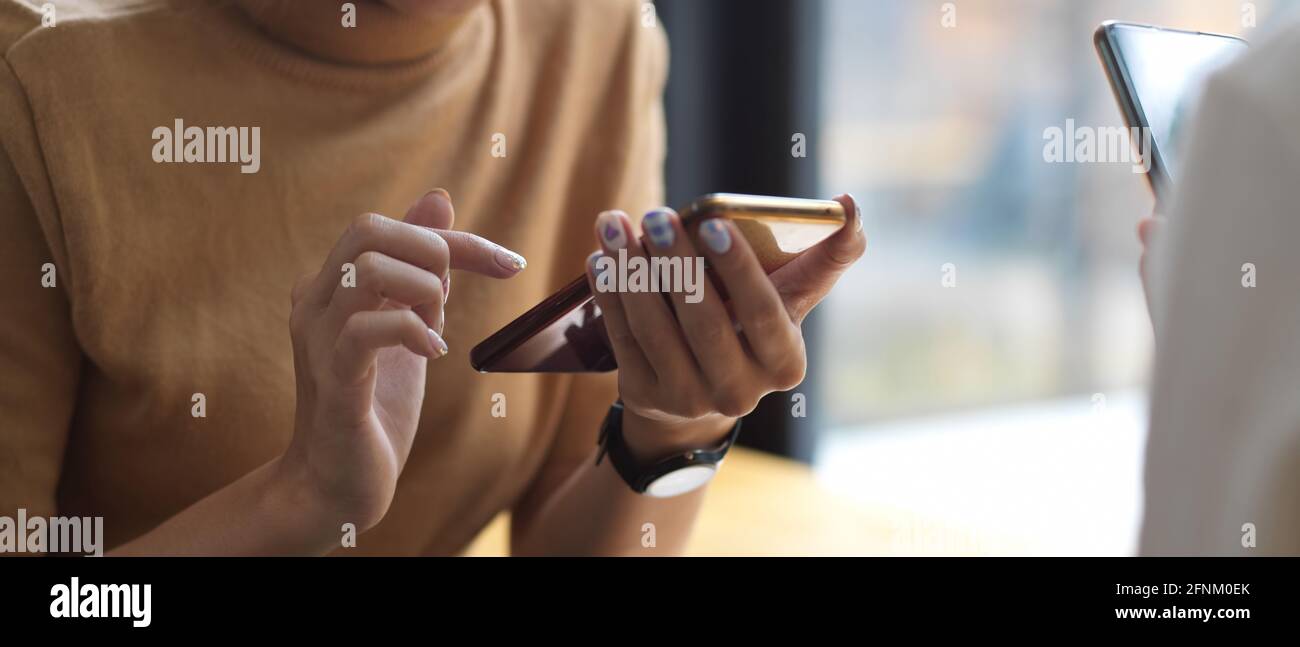 Close up view of two females using smartphone while sitting opposite ...