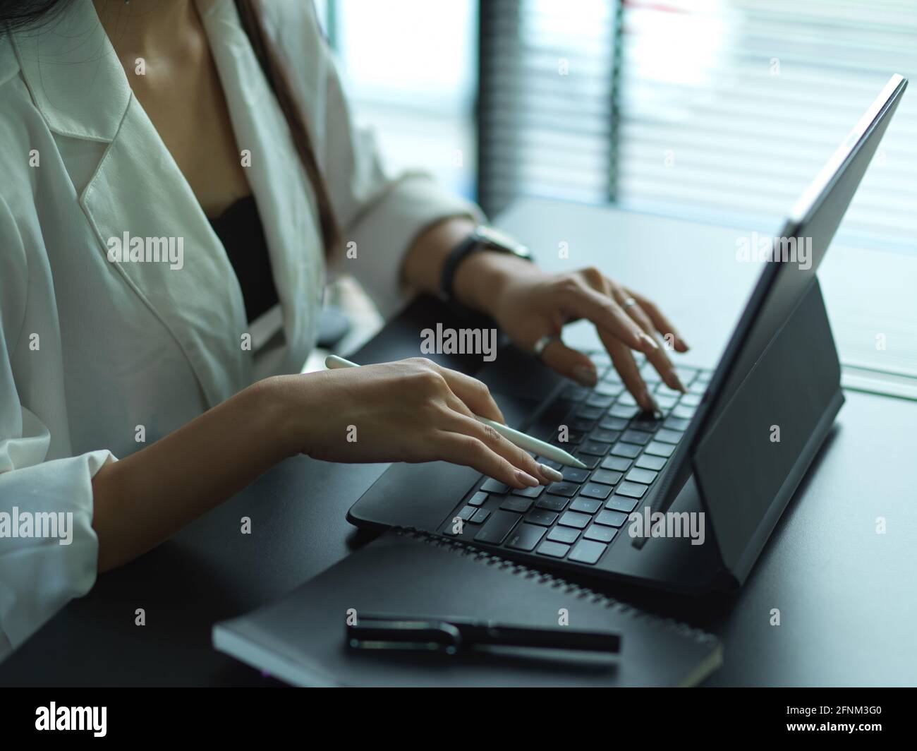 Side view of female hands typing on tablet keyboard with schedule book ...