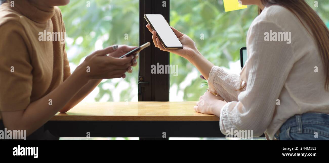 Cropped shot of two female teenagers using smartphone and talking to ...