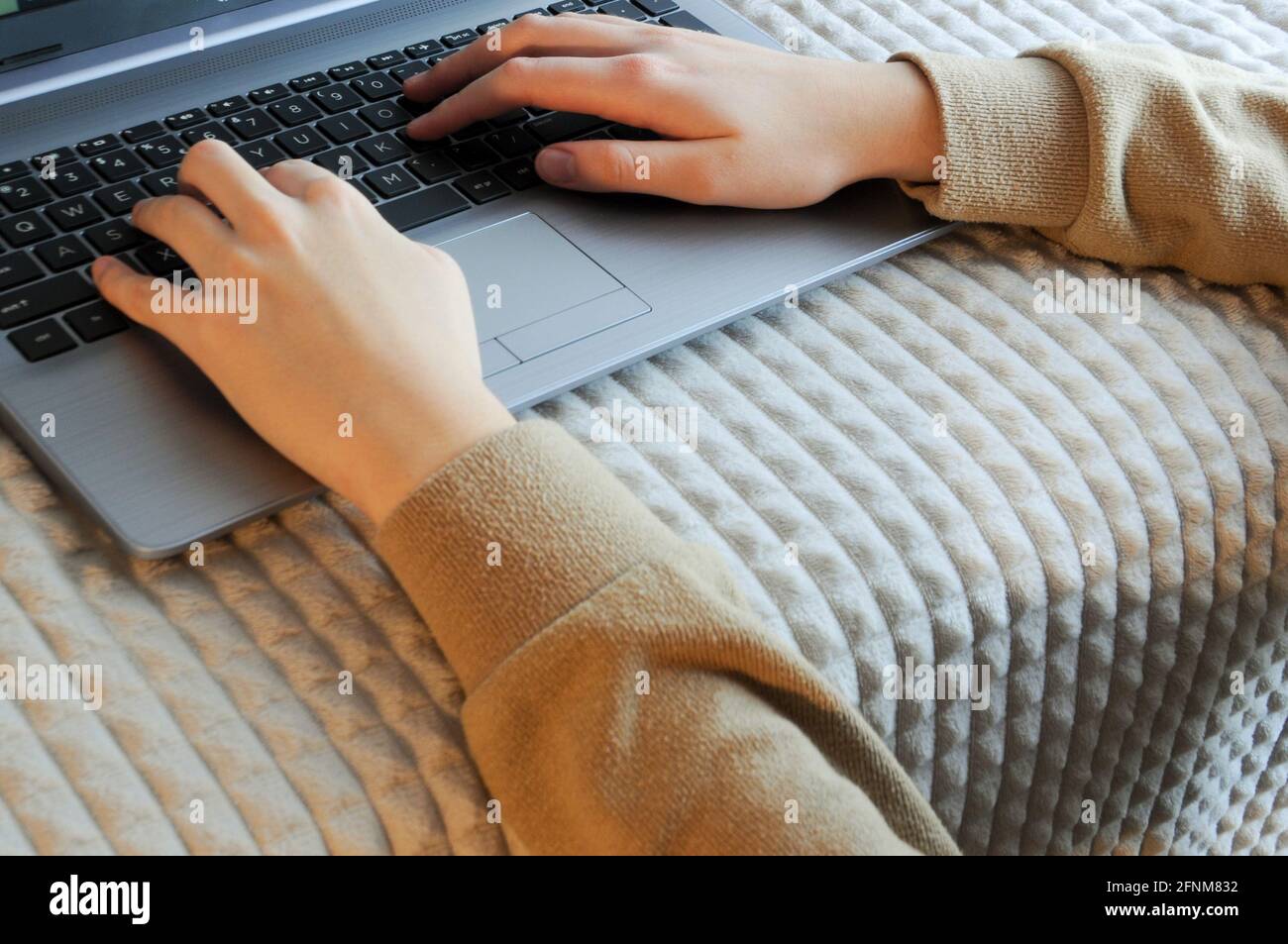 Person wearing brown sweatshirt, typing on a laptop keyboard on the bed ...