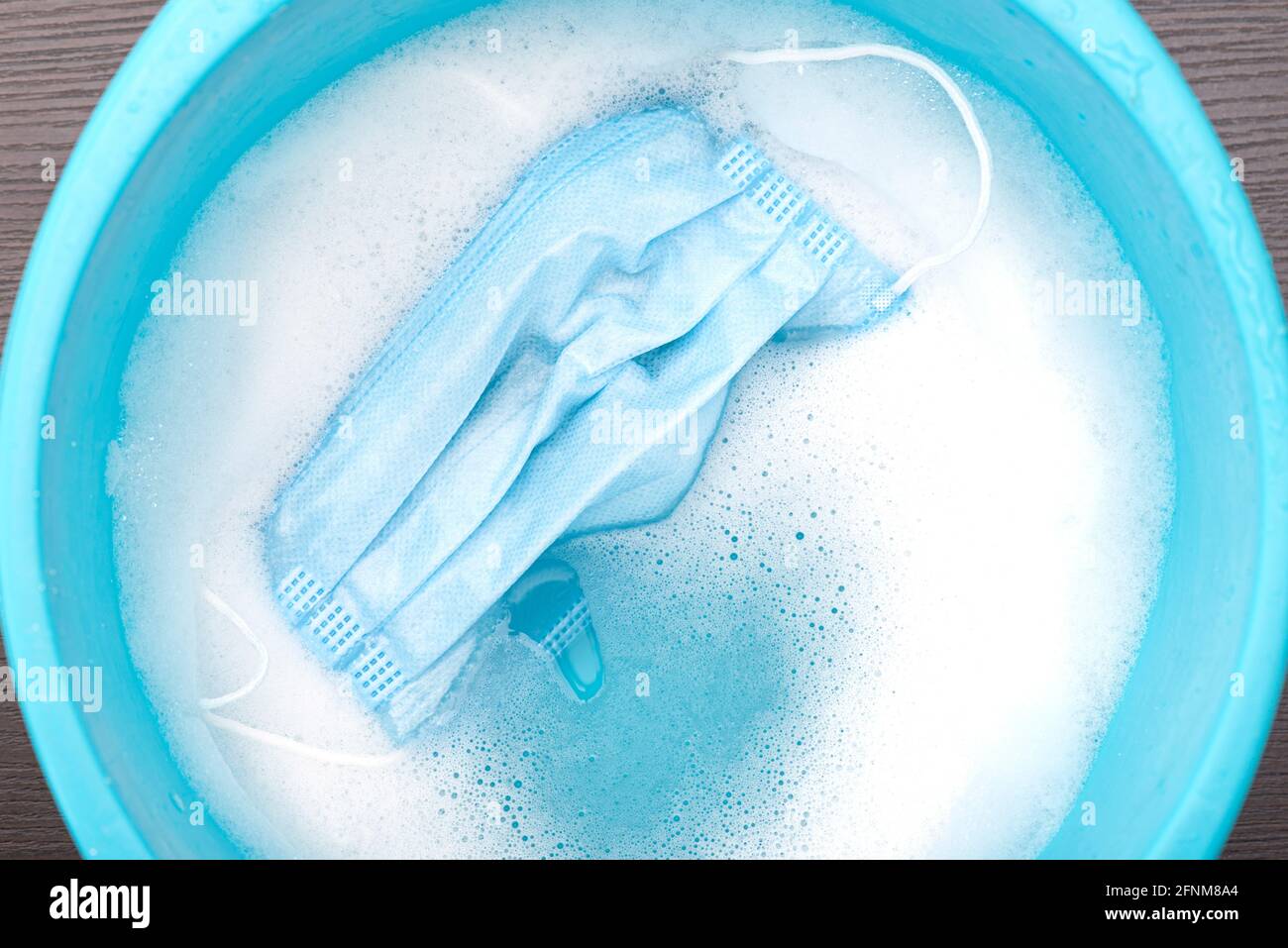 Disposable medical mask soaking in blue plastic basin with water with ...