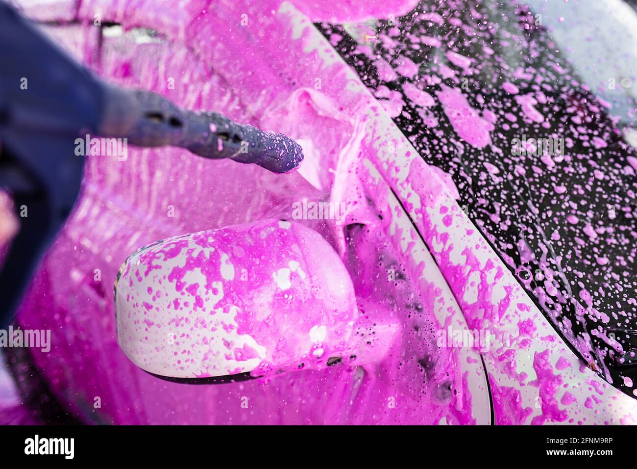 Gun sprinkles pink foam on car at self-service car wash. Unusual look ...
