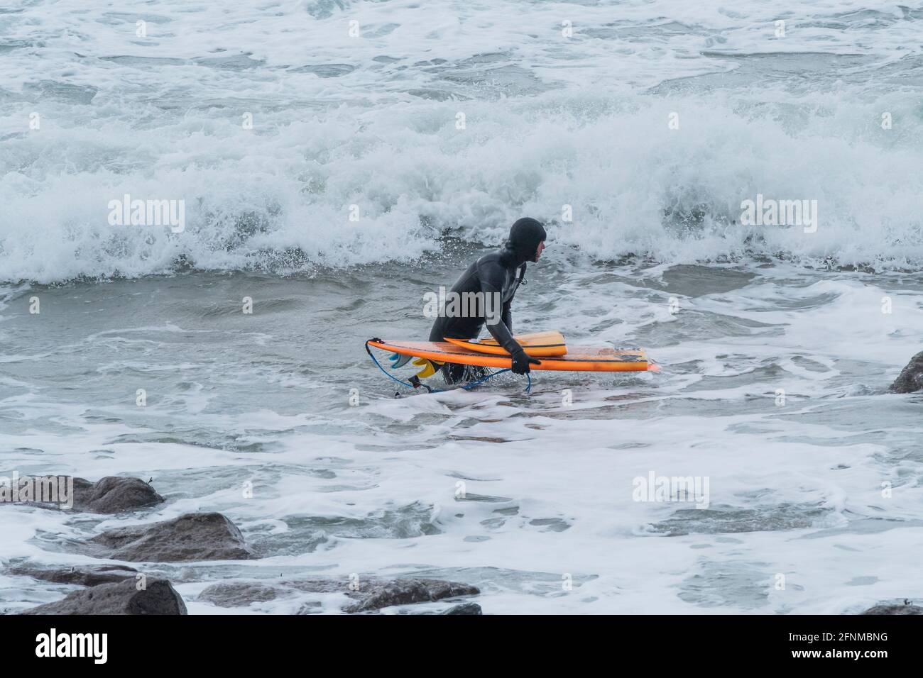 A surfer standing in the rough sea with a snapped surfboard at Little ...