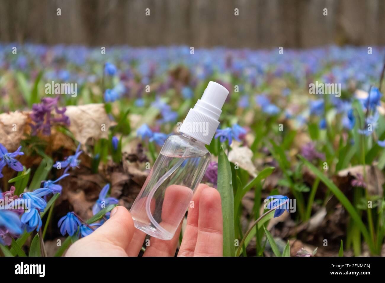 Hand holding clear liquid spray pump bottle in blooming pretty flower ...