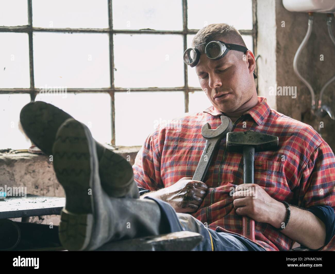 Young worker sitting on chair with legs on desk, holding hammer and ...