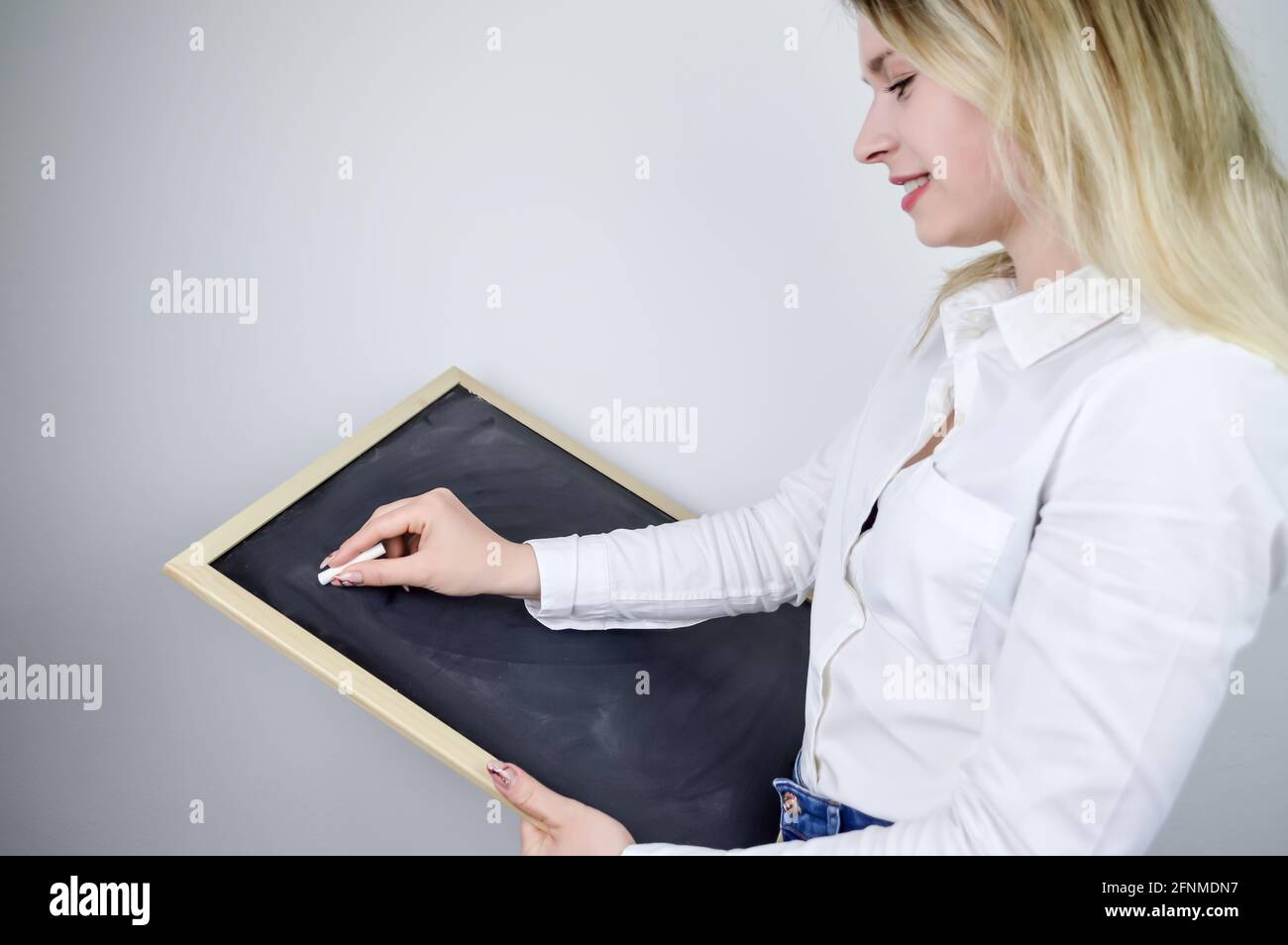 Portrait of a beautiful young blonde woman writing with chalk on a ...