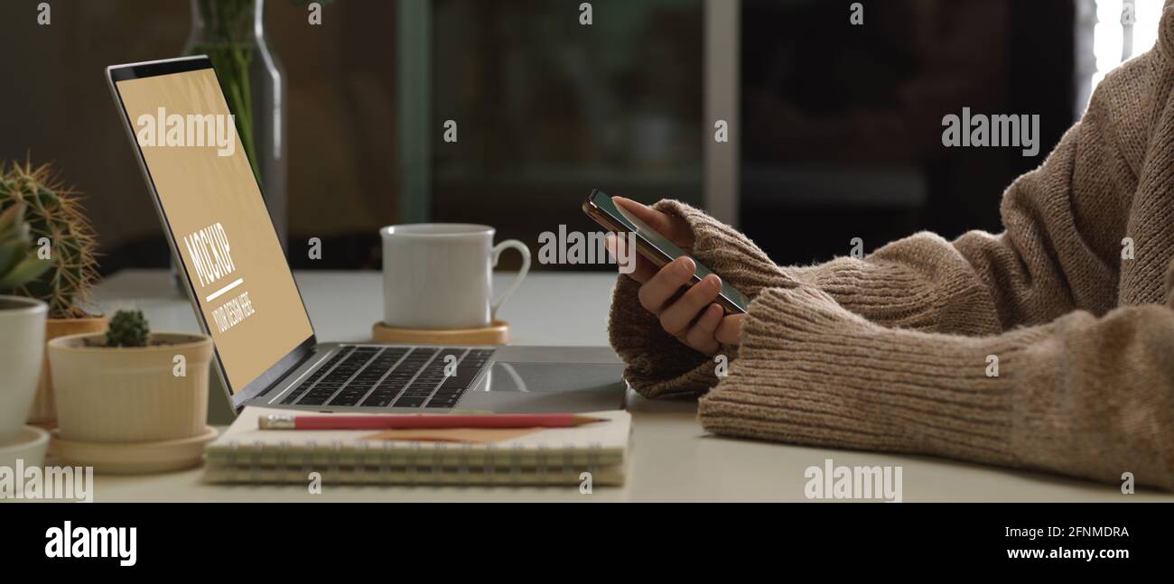 Side view of female hand holding smartphone while working with laptop ...