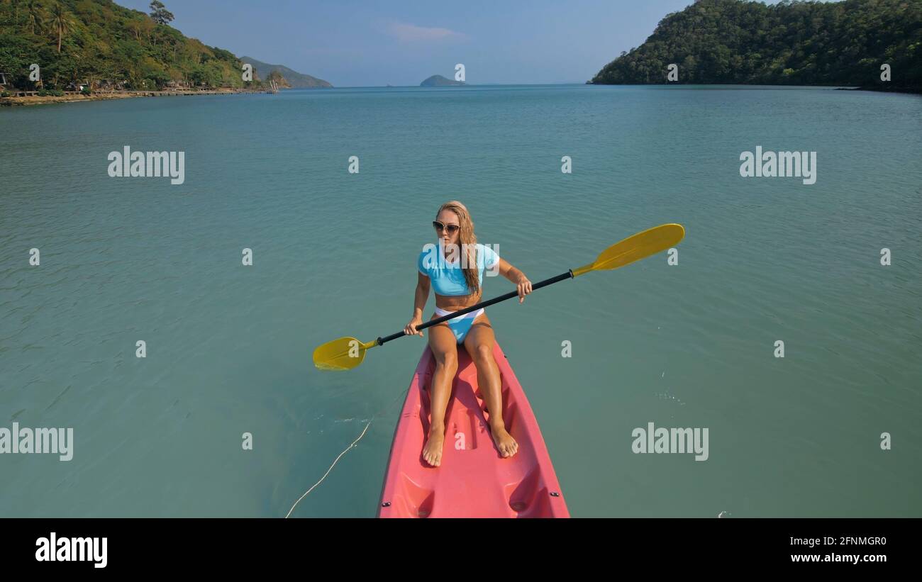 Pretty sportive blonde lady in stylish swimsuit sails on pink plastic ...