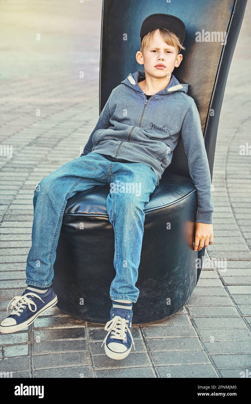 Adorable schoolboy in casual clothes and black cap rests sitting on ...