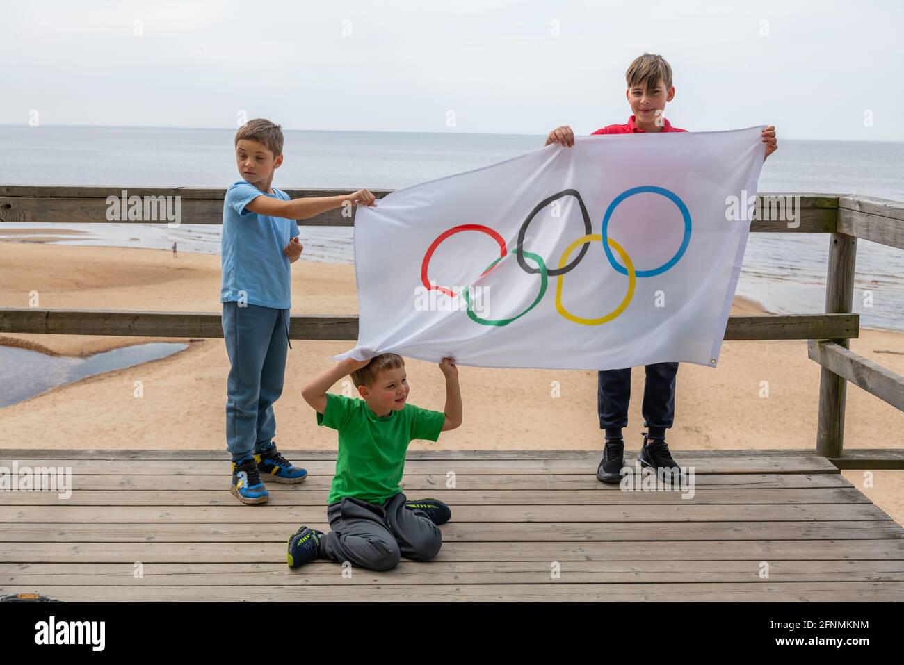 Riga, Latvia, May 16. 2021. Boys in green, red and blue t-shirts stay with flapping in wind flag ...