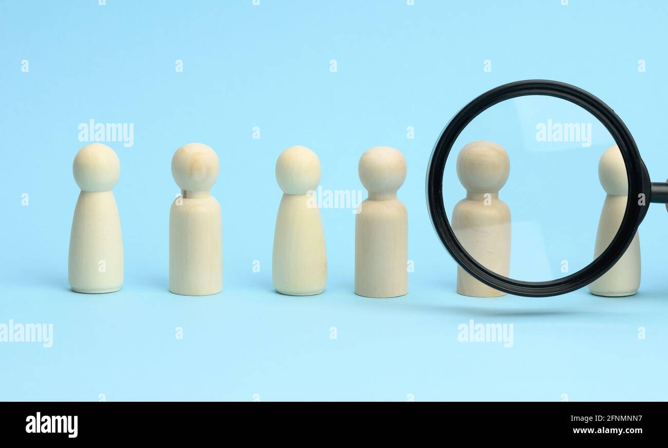 wooden figures of men stand on a blue background and a black magnifying ...
