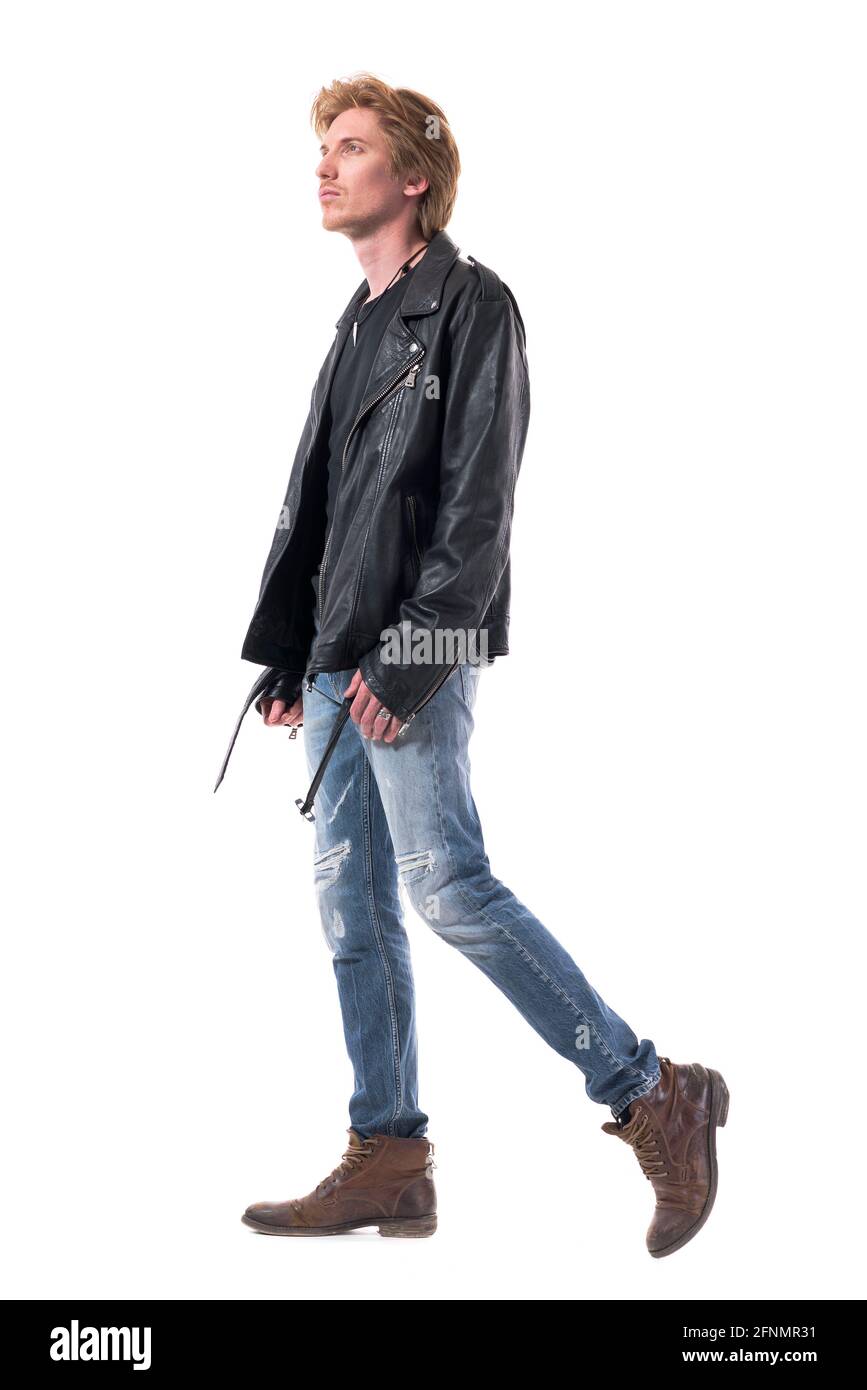 Side view of stylish rocker man walking in jeans and jacket looking up ...