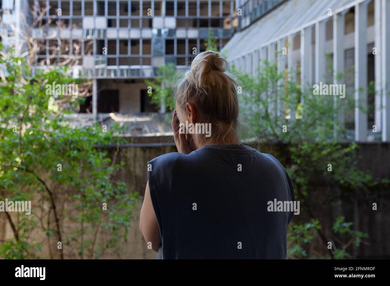 Blonde woman standing in front abandoned destroyed building, covering ...