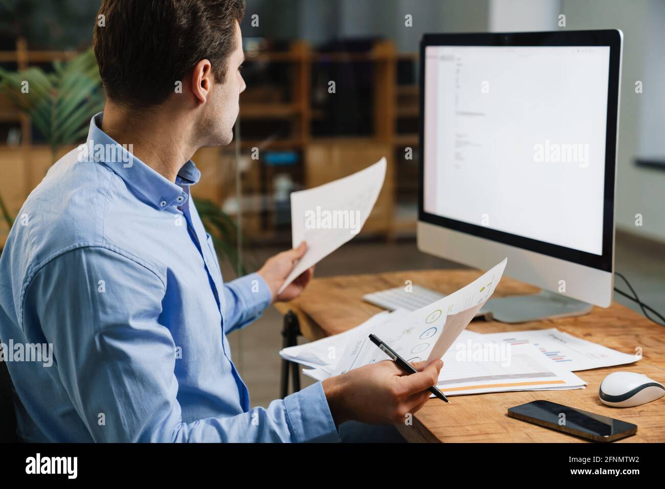 Pensive attractive young entrepreneur looking through paperwork while ...