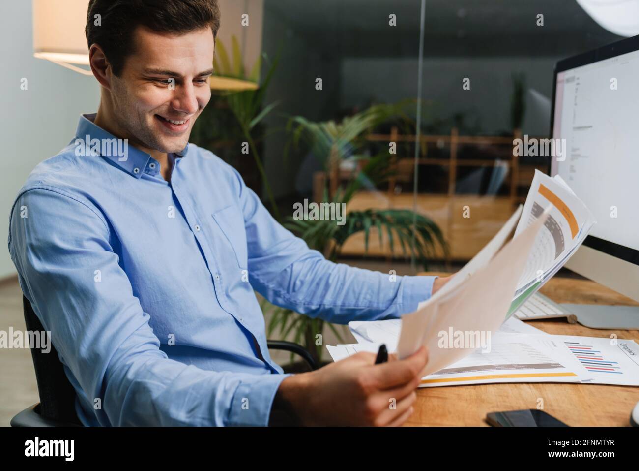 Happy cheerful young man celebrating success while sitting in the ...