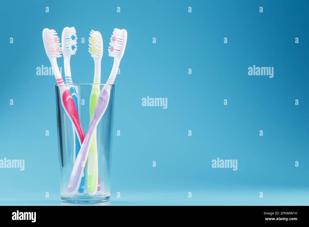 Toothbrushes of different colors in a transparent glass on a blue ...