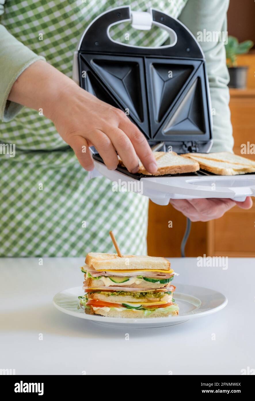 Hands hold toaster with fried fresh slices of bread near ready sandwich ...