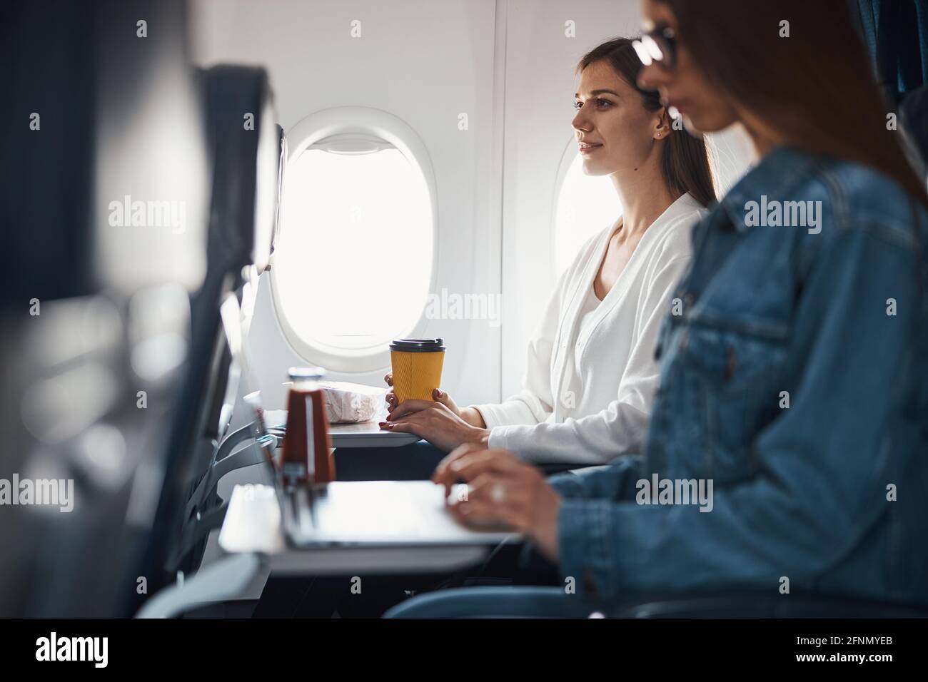 Female with coffee near her friend with laptop on airplane Stock Photo ...
