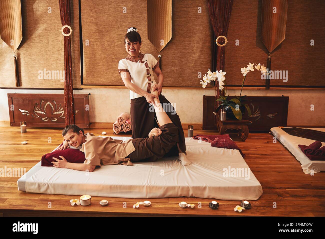 Thai massage worker pulling left leg of woman to side Stock Photo - Alamy