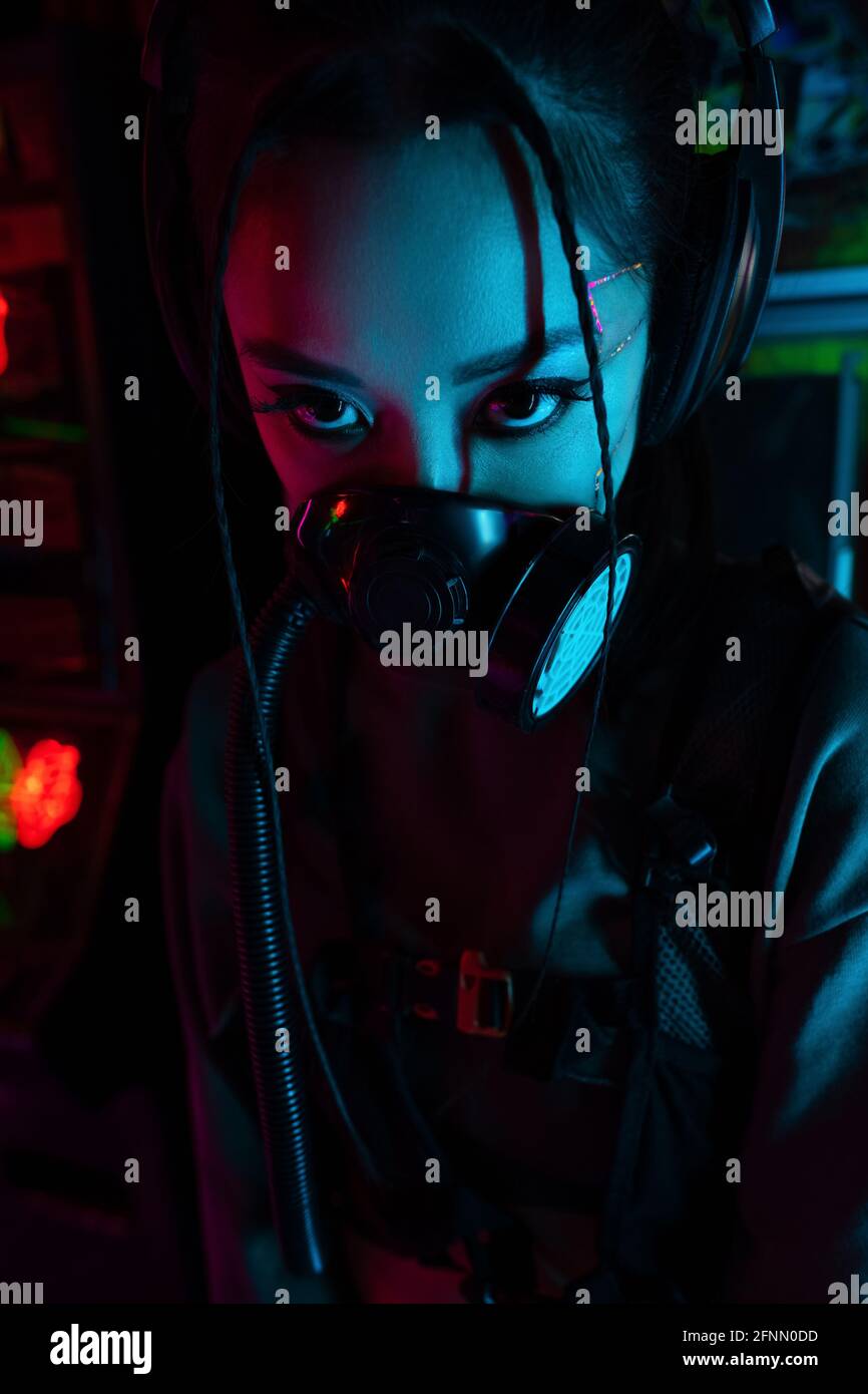 young asian woman with scar in gas mask and wireless headphones looking ...