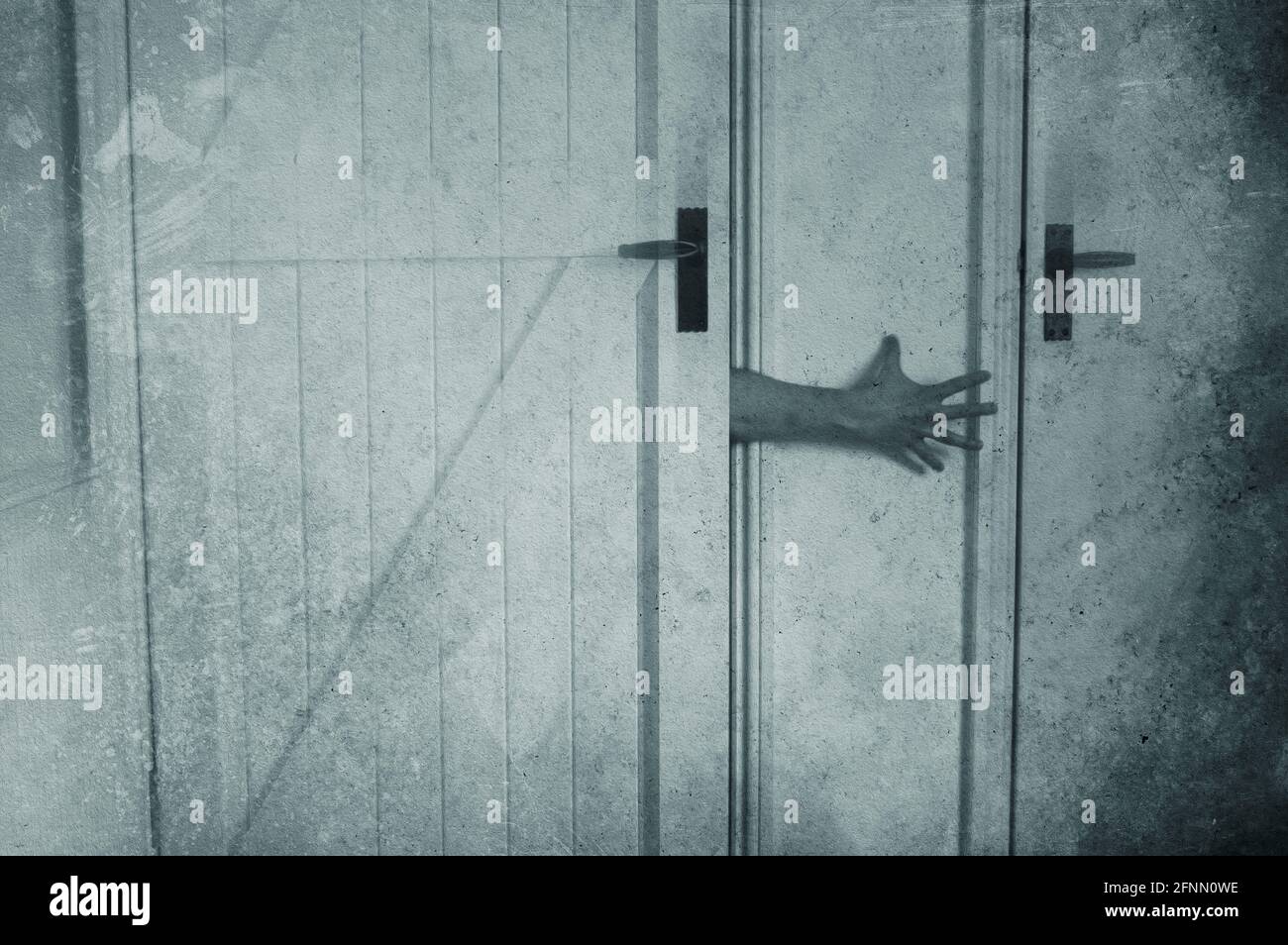 A horror concept of a spooky arm coming out of an old wooden door in a ...