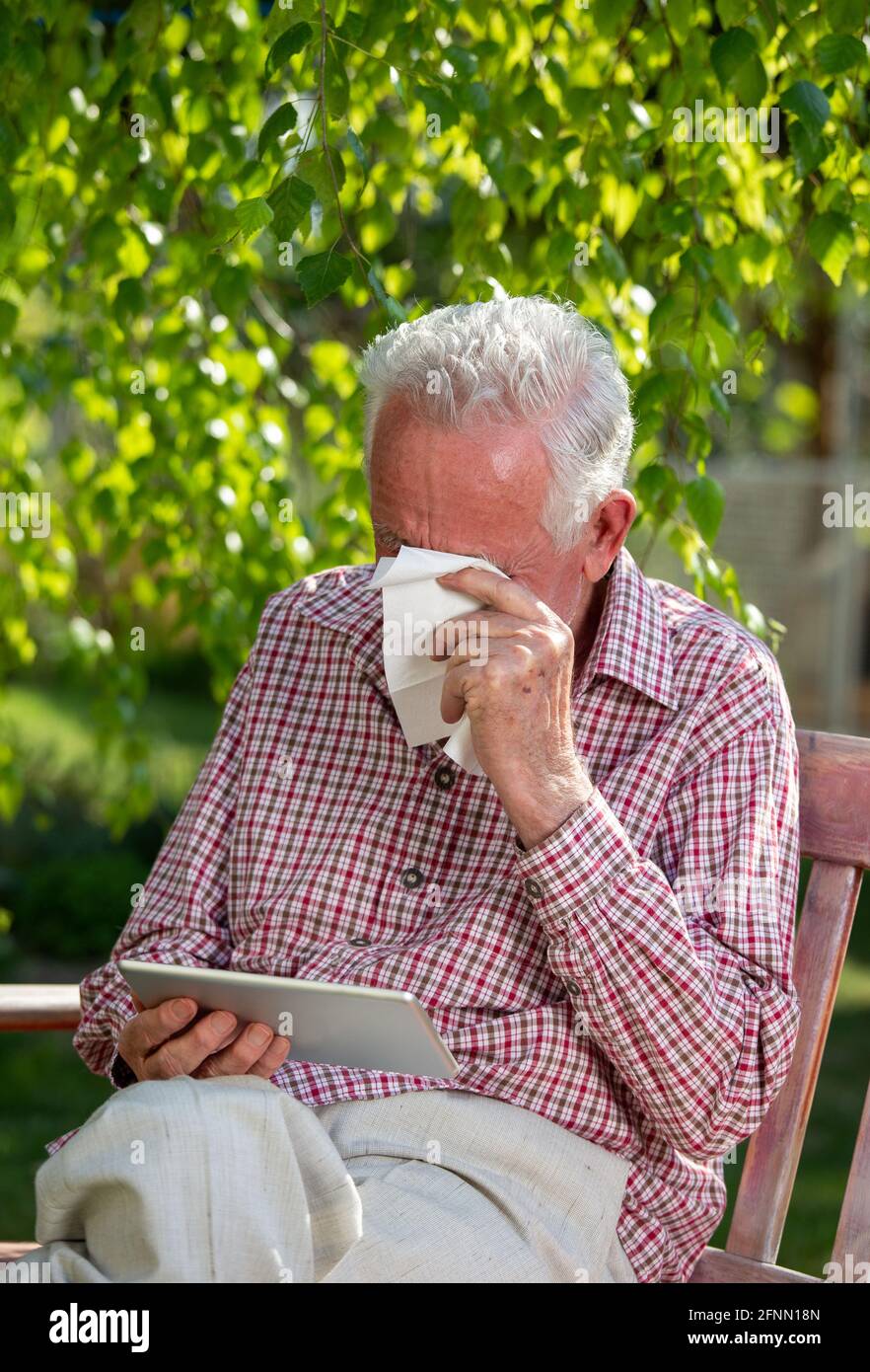 Senior man looking at tablet crying and holding tissue over mouth in ...