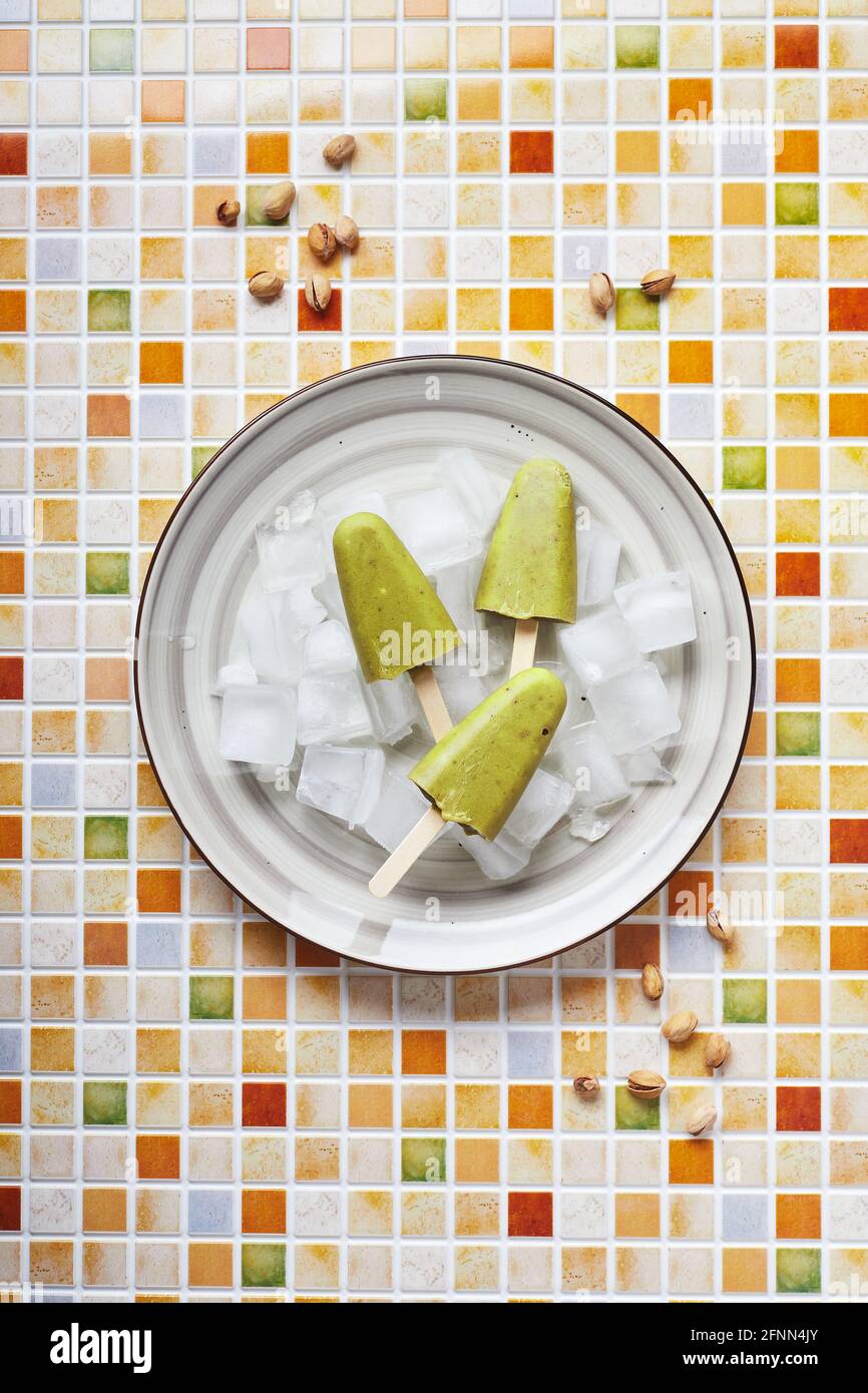 Frozen homemade pistachio popsicle in bowl of ice on mosaic tile table ...