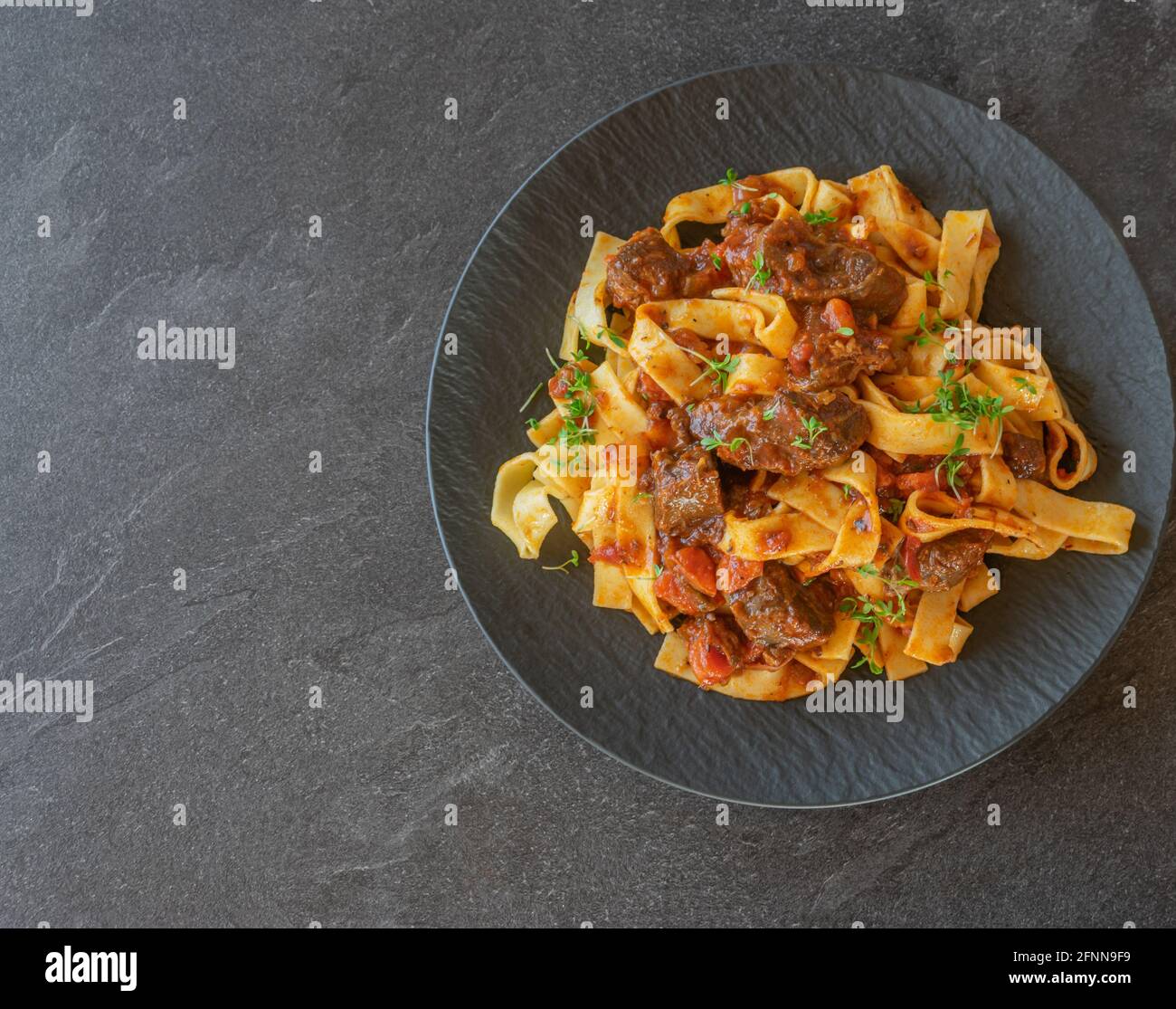 Pasta with italian beef stew served on a dark plate on dark table ...