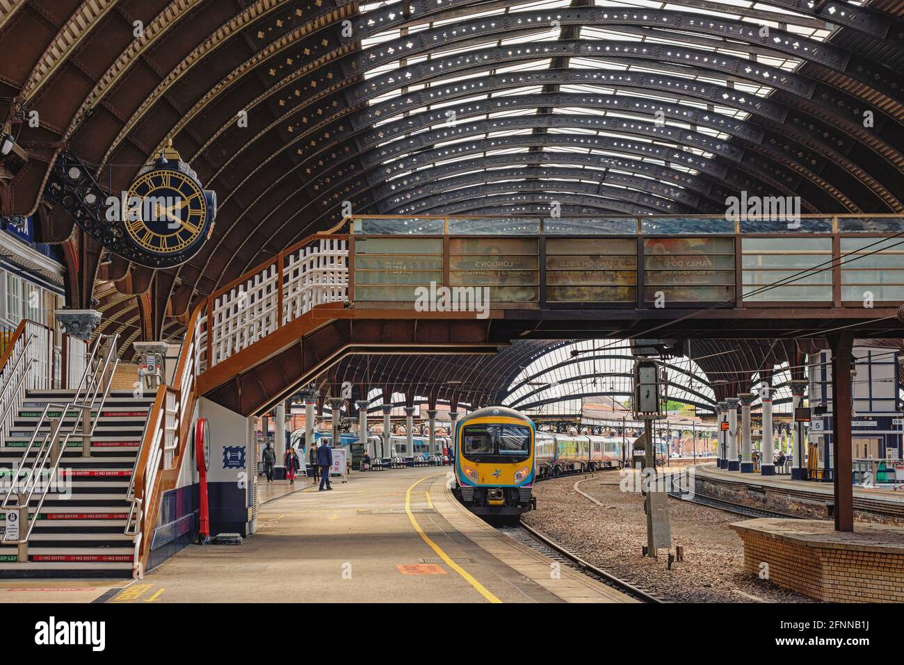 A train stands at a platform of a railway station. A footbridge crosses ...