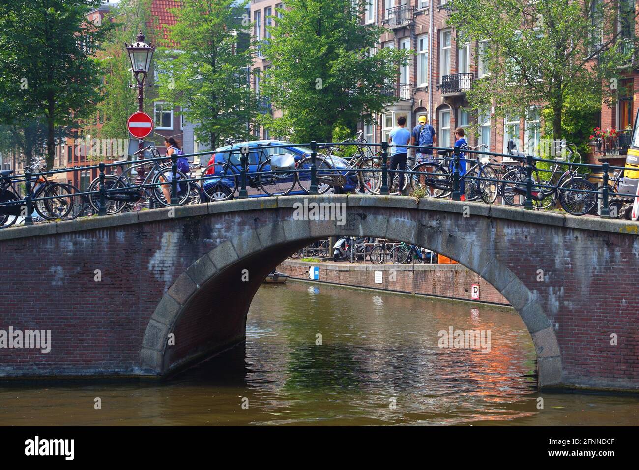 AMSTERDAM, NETHERLANDS - JULY 7, 2017: People cross a canal bridge in ...