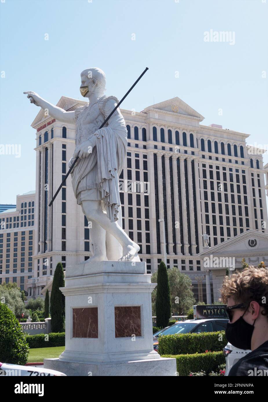A young man wearing a face mask walking by a statue of Julius Caesar ...