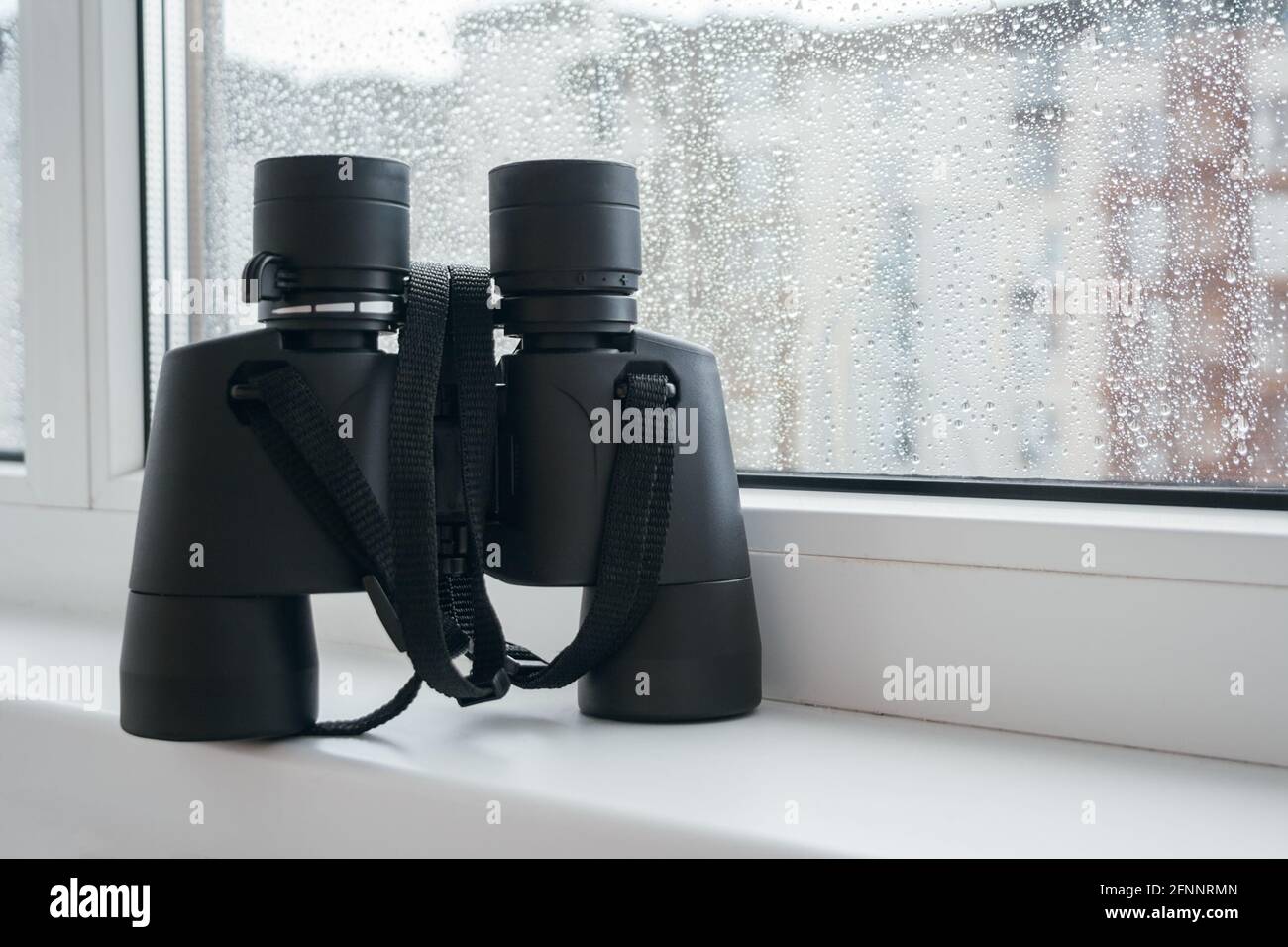 Black binoculars for observing neighbors is on a white window sill by ...