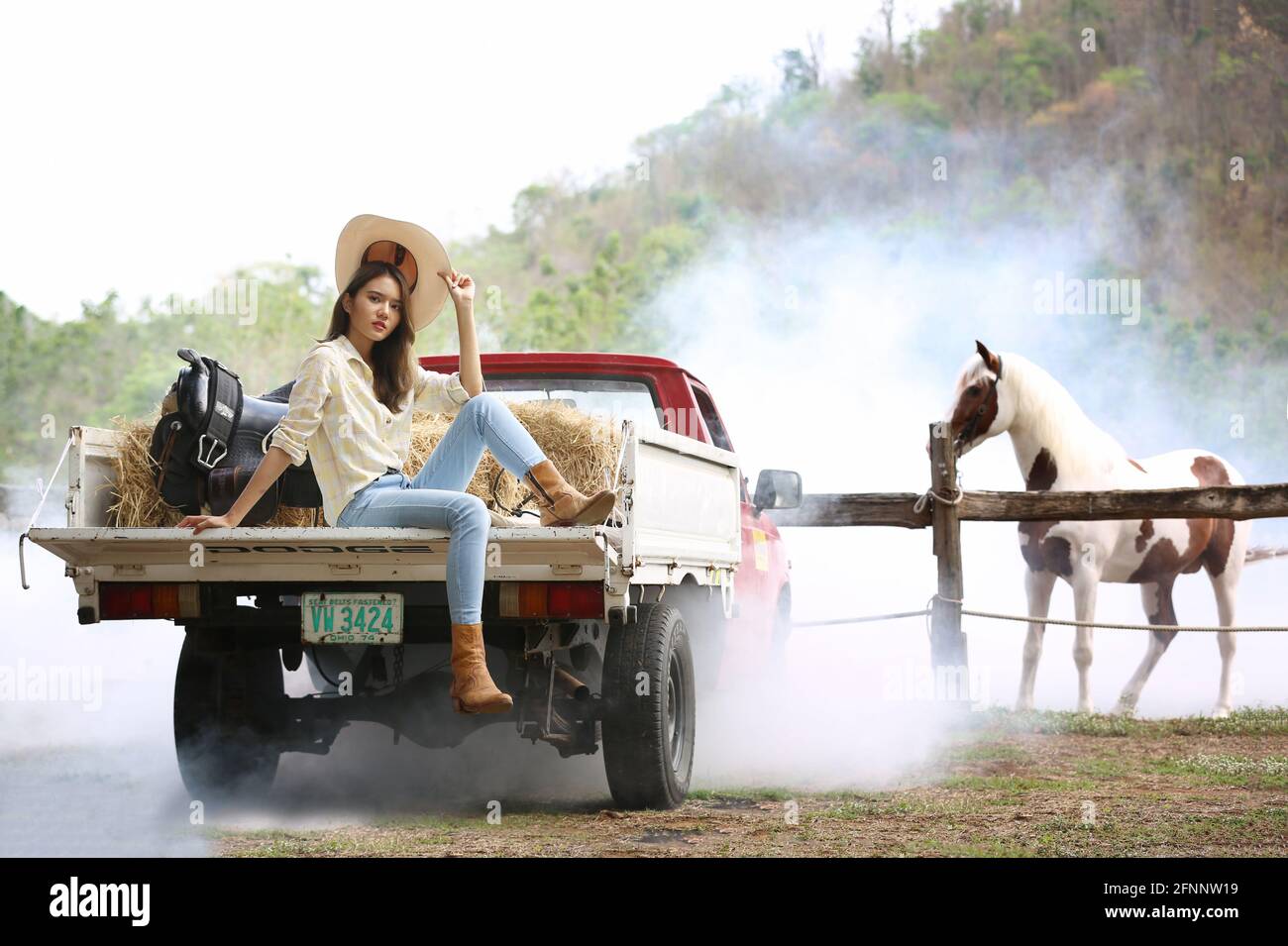 A woman in a cowgirl style sits in a horse ranch with a western farm ...