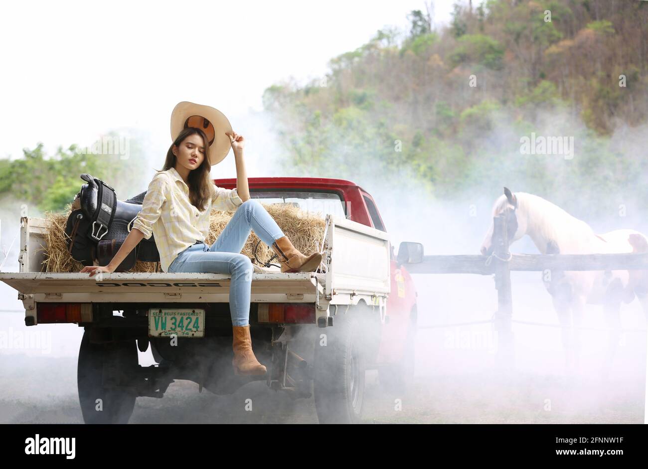 A woman in a cowgirl style sits in a horse ranch with a western farm ...