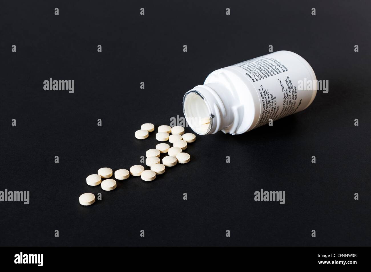 Vitamin tablets spilling out of an open white plastic container on a ...