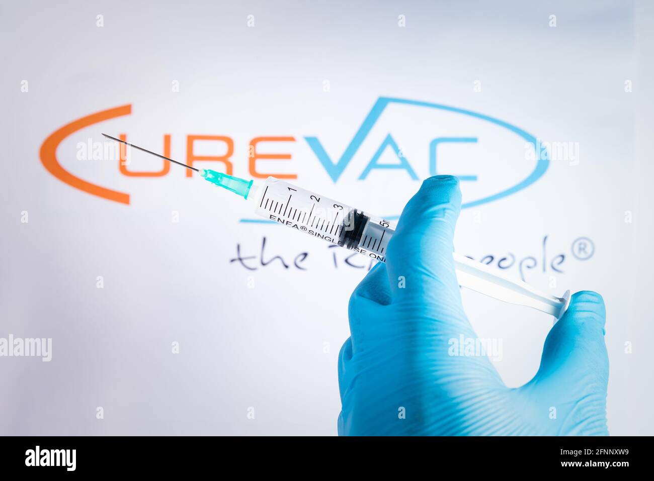 A hand holds a syringe in front of Curevac vaccine logo in Barcelona ...