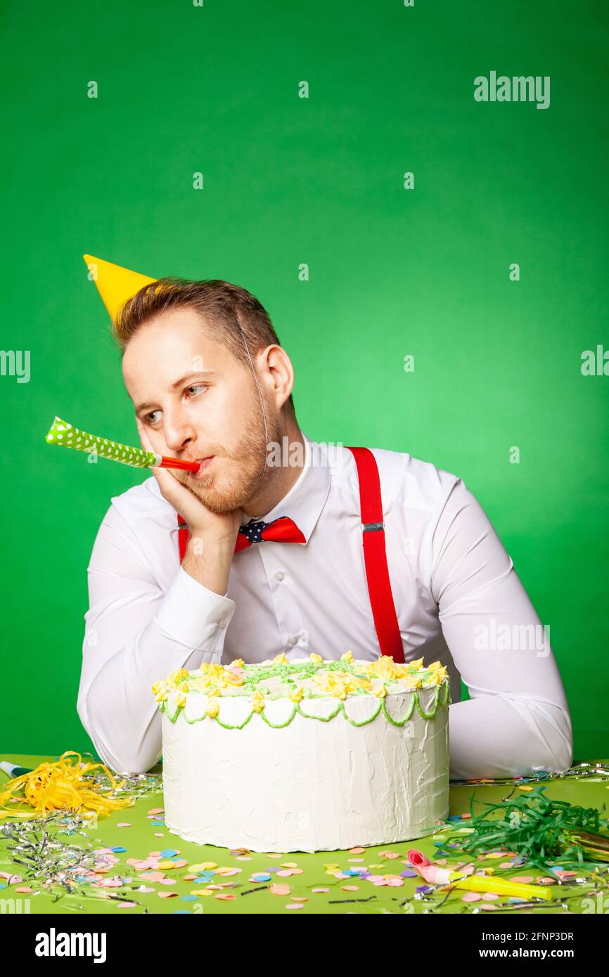 Sad man in party hat sitting at table with sweet birthday cake and ...