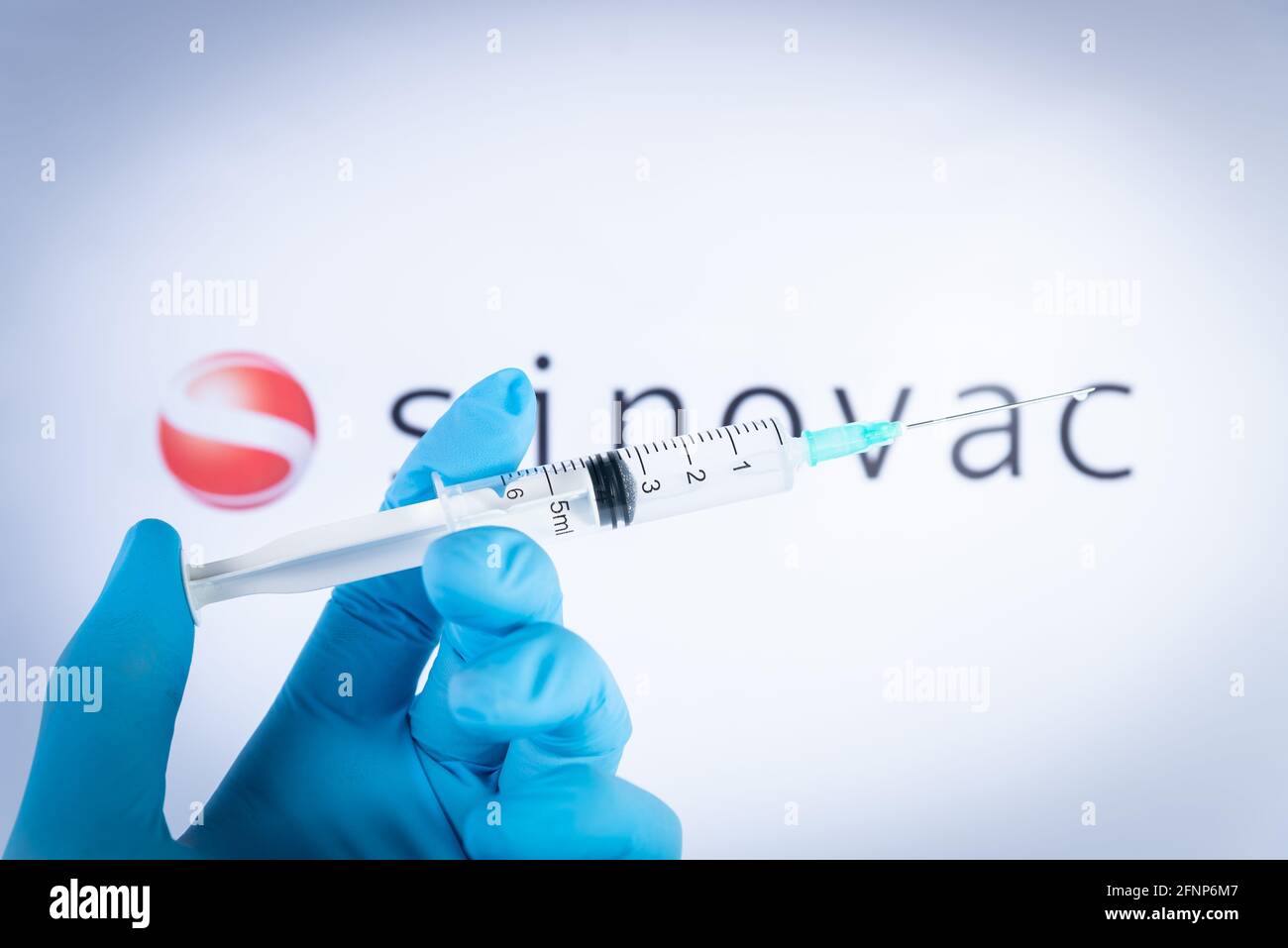 A hand holds a syringe in front of Sinovac vaccine logo in Barcelona ...