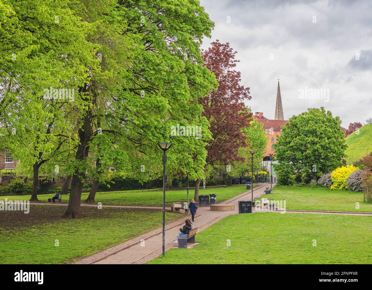 Public gardens where two paths cross quartering the lawn. Trees display ...