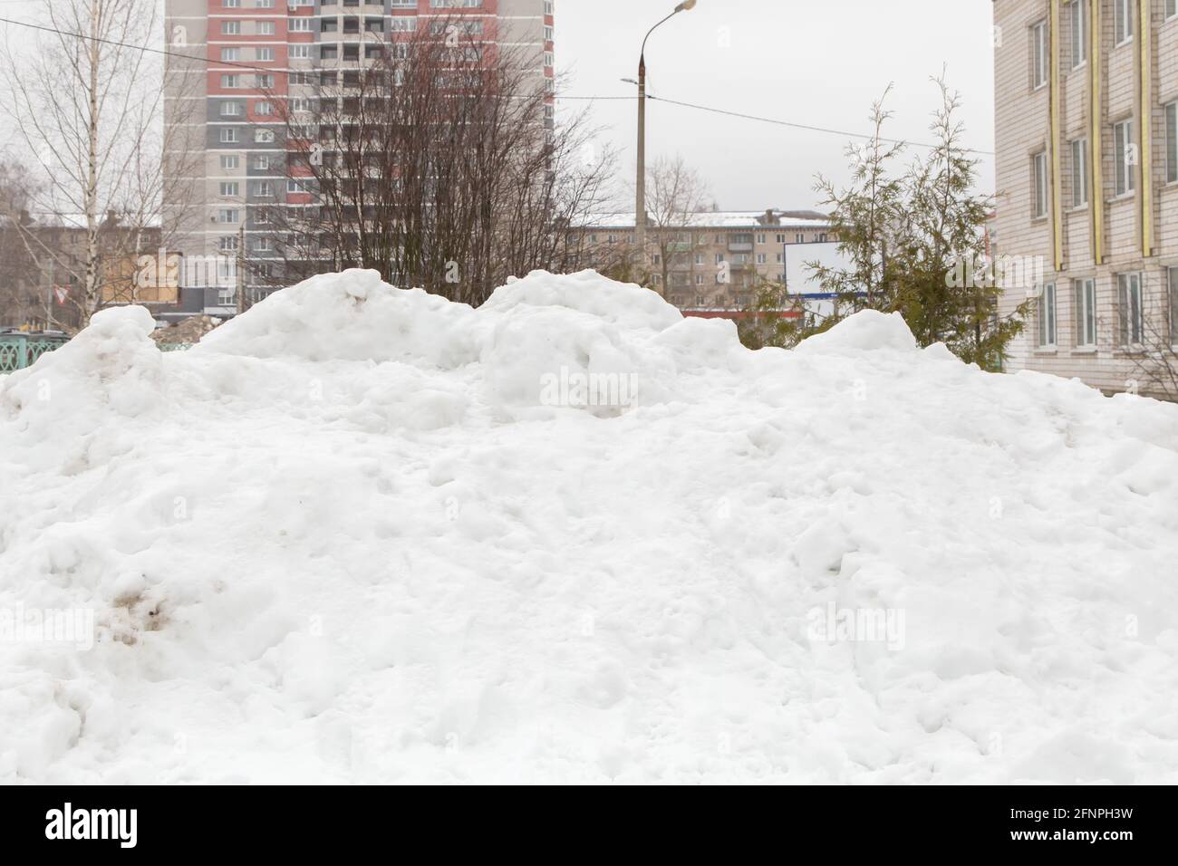 A large snowdrift on a city street with high-rise buildings. A block of ...