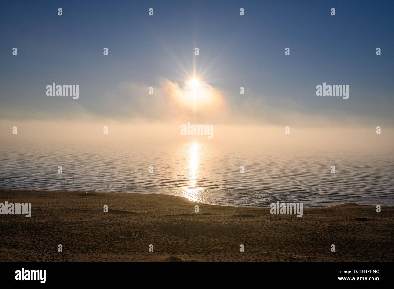 Star like sun with rays of light behind fog on sea at sunset with calm ...
