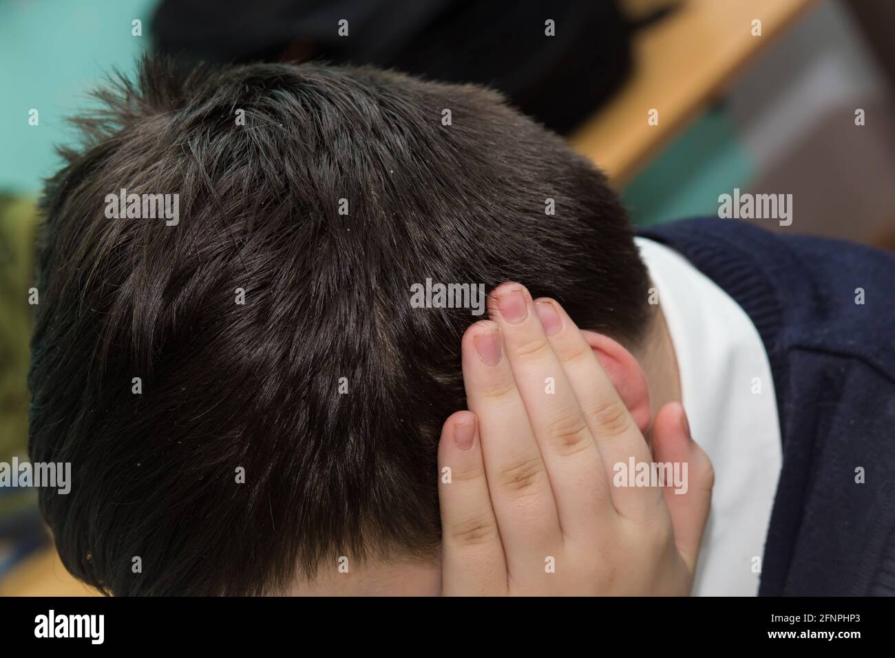 Close-up of a boy's hand supporting his head at the temple. A student ...